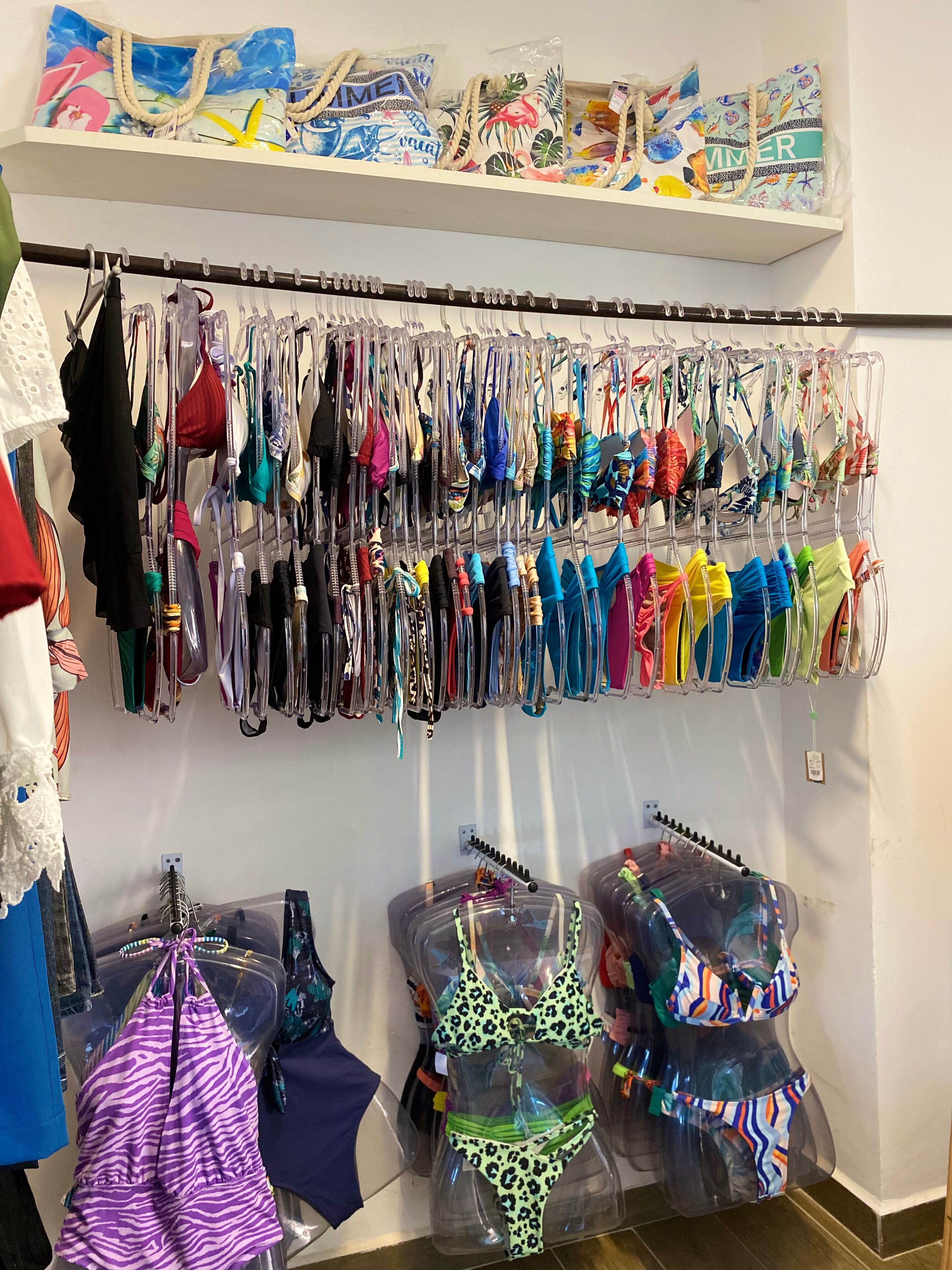 Uma loja de roupas com diversos artigos de roupa de banho expostos em araras e recipientes de plástico transparente.