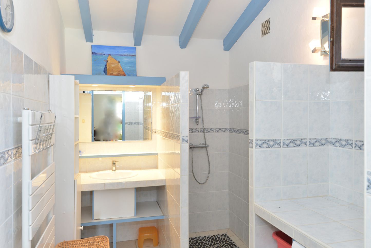 Casa de banho com lavatório, espelho, chuveiro e um pequeno banquinho.