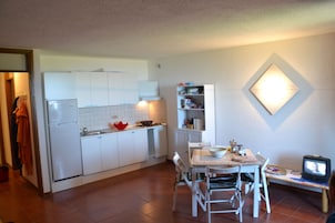 Uma cozinha compacta com armários brancos, uma mesa de jantar com cadeiras, uma televisão pequena e um aplique de parede.