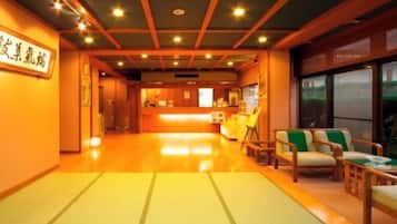 Interior de uma pousada japonesa tradicional, com piso de tatame, mobiliário de madeira e balcão de recepção.