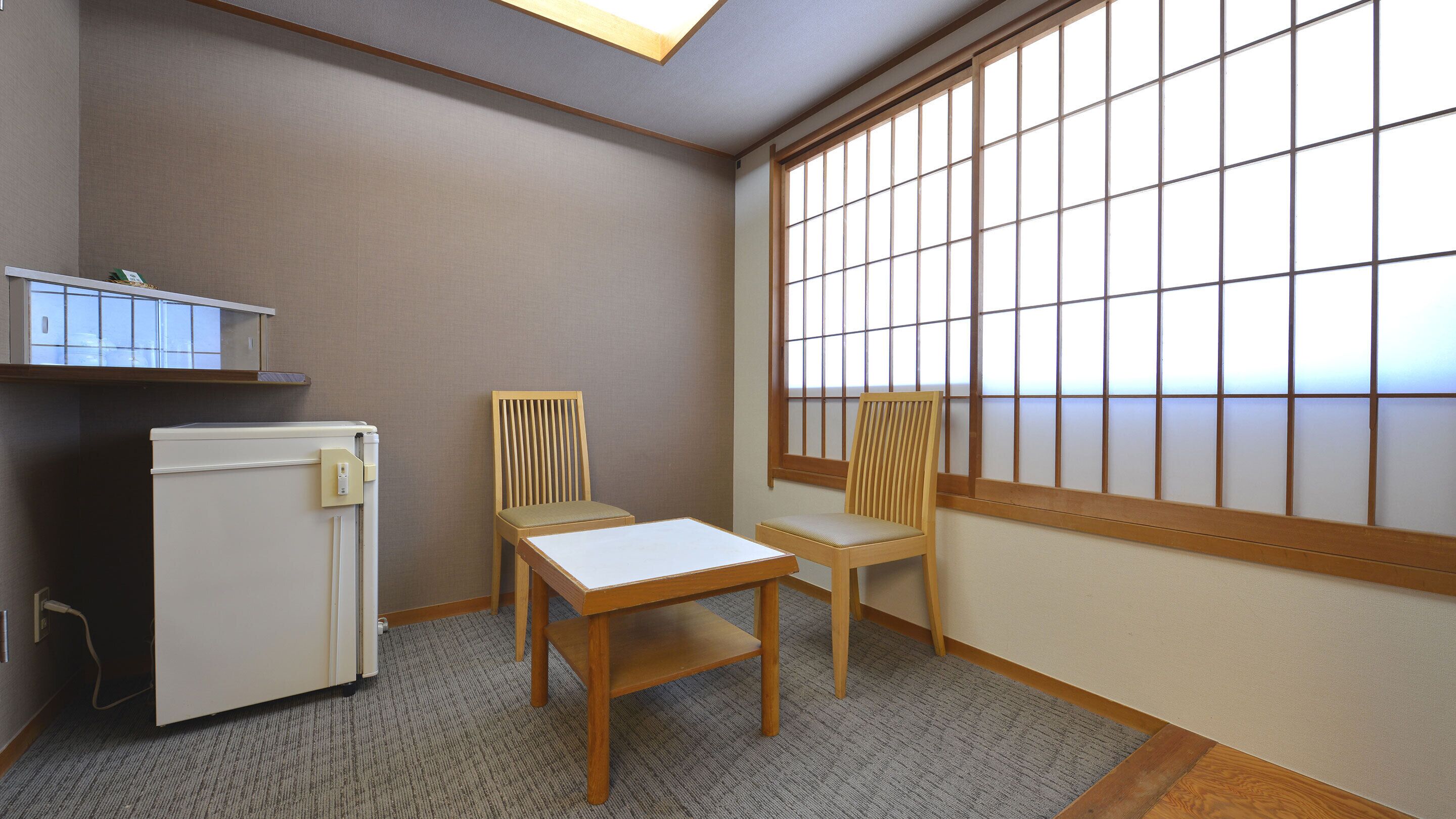 Um quarto pequeno com uma janela de estilo tradicional japonês, um frigorífico branco e duas cadeiras de madeira.