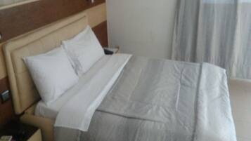Quarto de hotel com cama, mesa de cabeceira e luminária na parede.