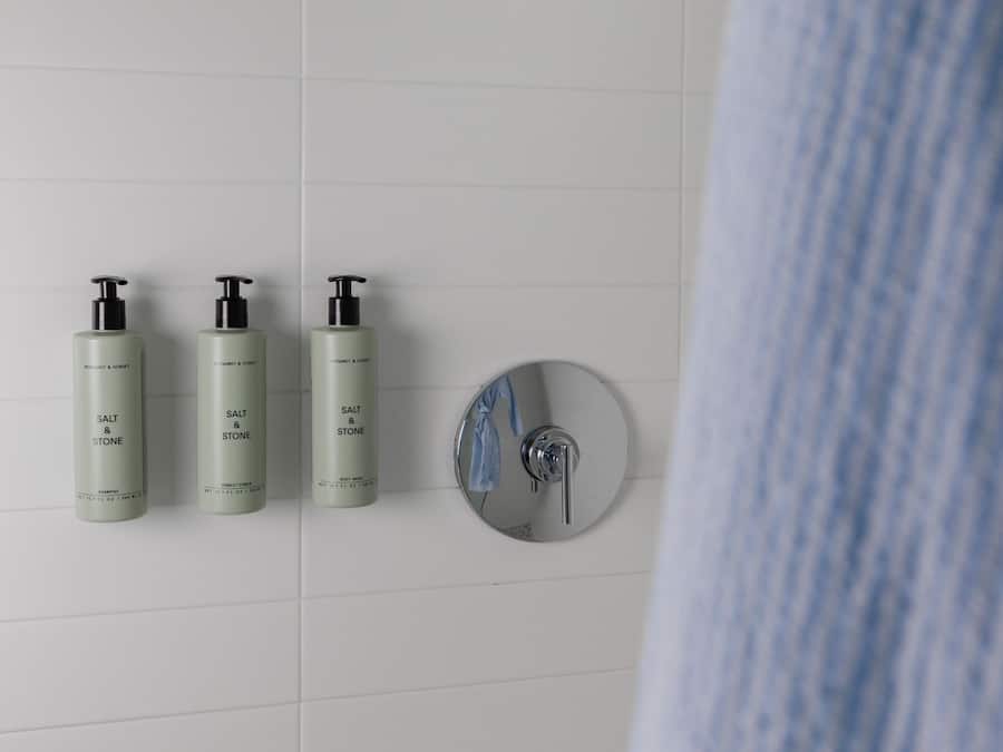 Três frascos de shampoo e condicionador sobre uma parede com azulejos brancos.