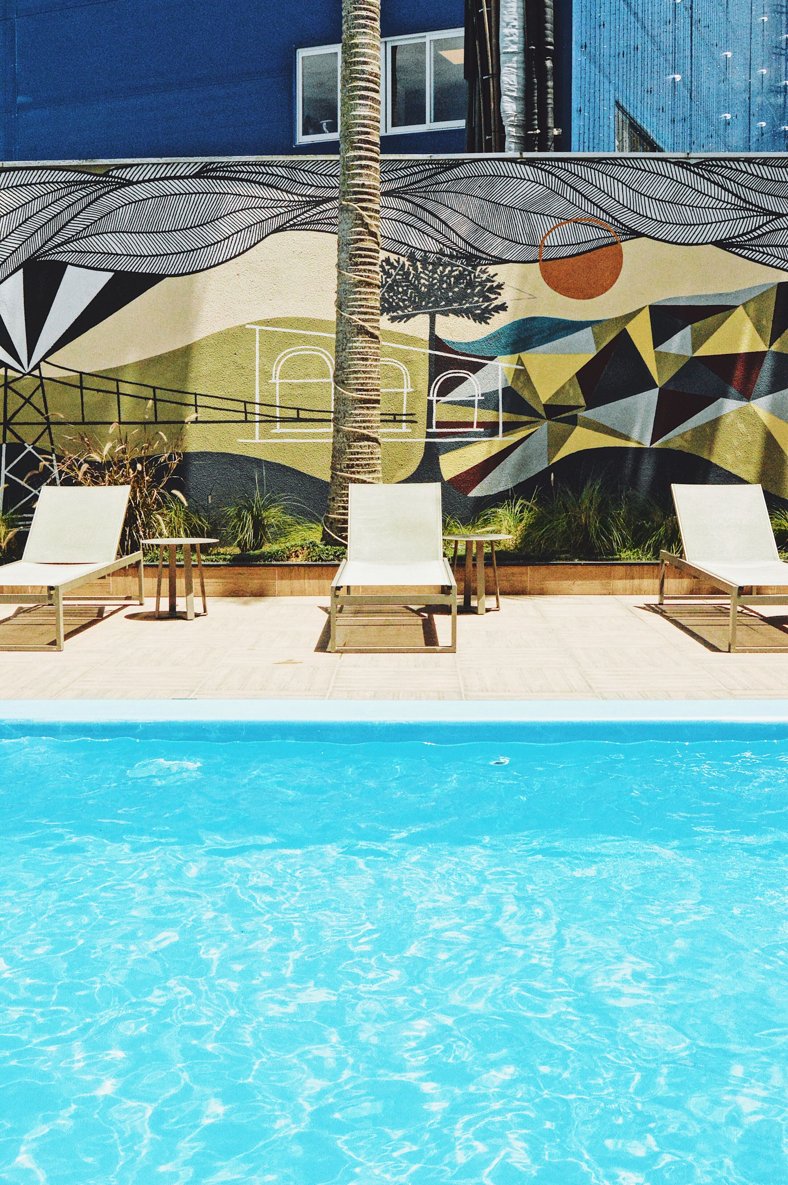 Área da piscina com espreguiçadeiras e um mural na parede.