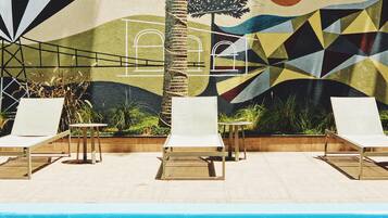 Área da piscina com espreguiçadeiras e um mural na parede.