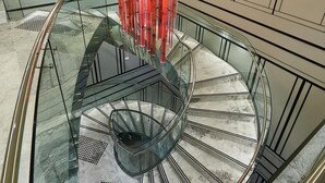 Uma escada espiral moderna com guarda-corpos de vidro e um pilar central, emoldurada por um design de parede minimalista.
