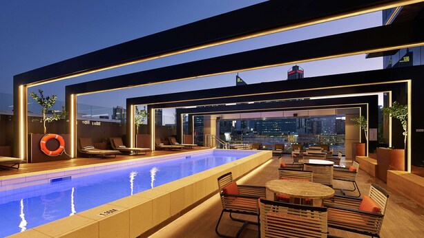 Uma área de piscina no terraço com vista para o horizonte da cidade, espreguiçadeiras e mesas.
