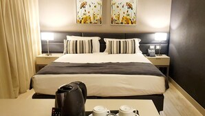 Quarto de hotel com cama, mesas de cabeceira, bandeja para café com chávenas e chaleira, e duas pinturas nas paredes.