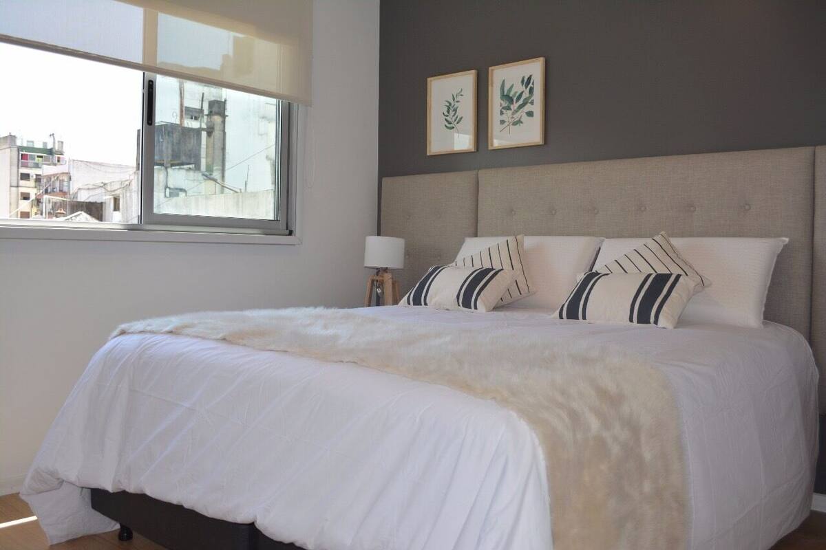 Quarto com cama grande, janela e duas imagens emolduradas na parede.