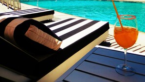 Uma área de descanso à beira da piscina, com espreguiçadeiras listradas e um copo de bebida de laranja.