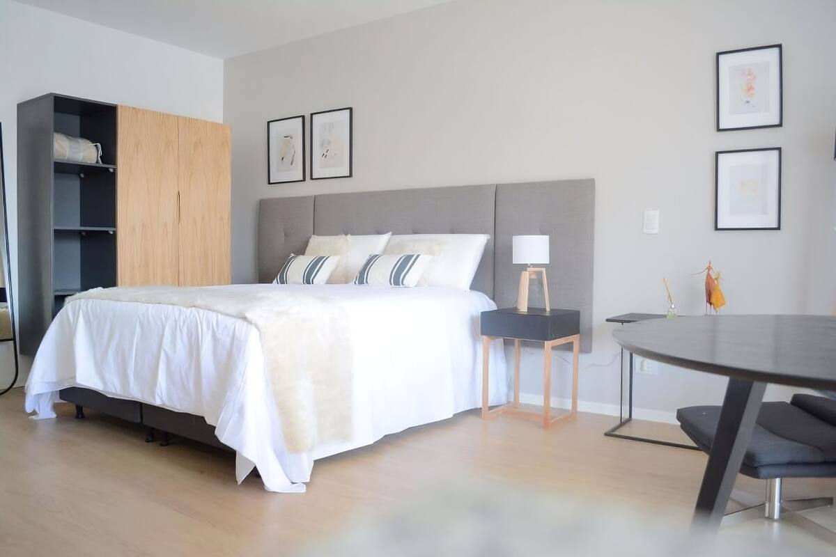 Quarto moderno com cama, mesa de cabeceira, abajur e uma pequena mesa redonda.