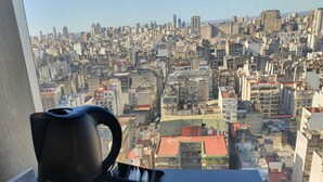 Uma mesa com uma bandeja contendo duas xícaras de café e uma cafeteira, com vista para o horizonte da cidade.