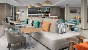 Um hall de hotel moderno com área de estar, um canto de café e uma TV fixada na parede.