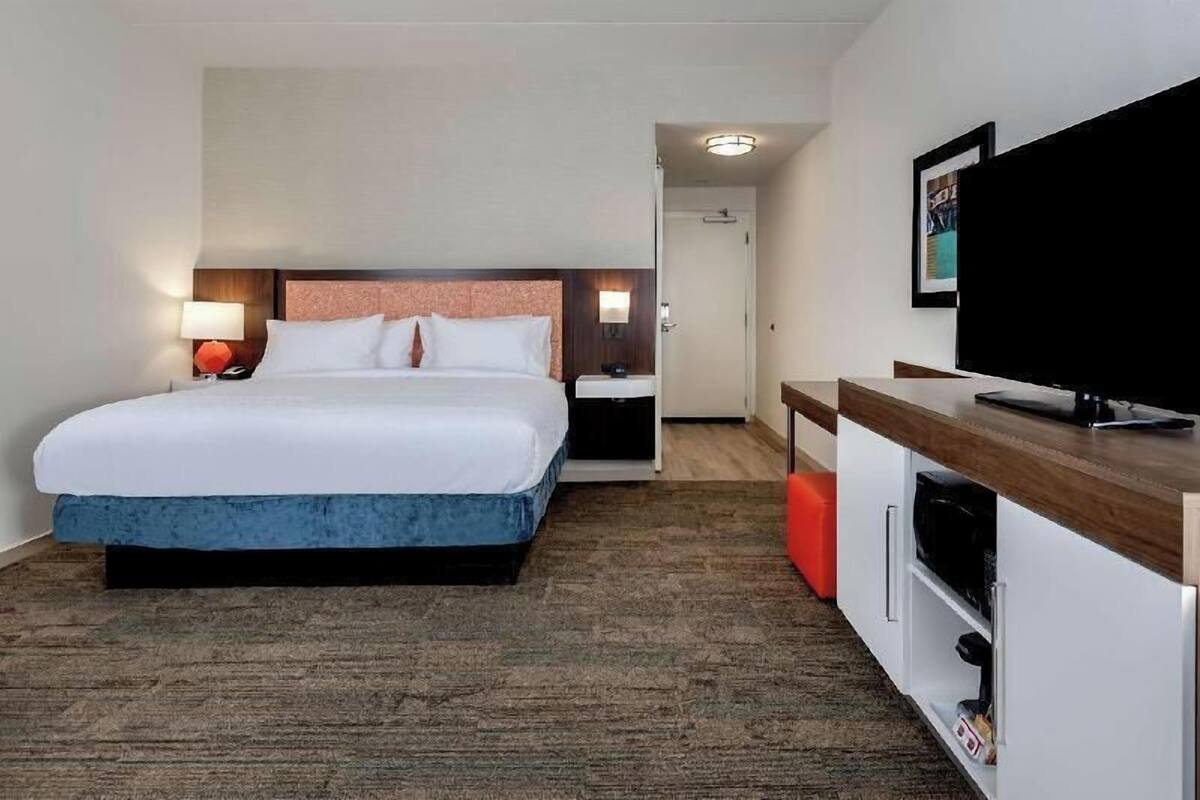 Quarto de hotel com cama, televisão, escrivaninha e porta que dá para outro espaço.