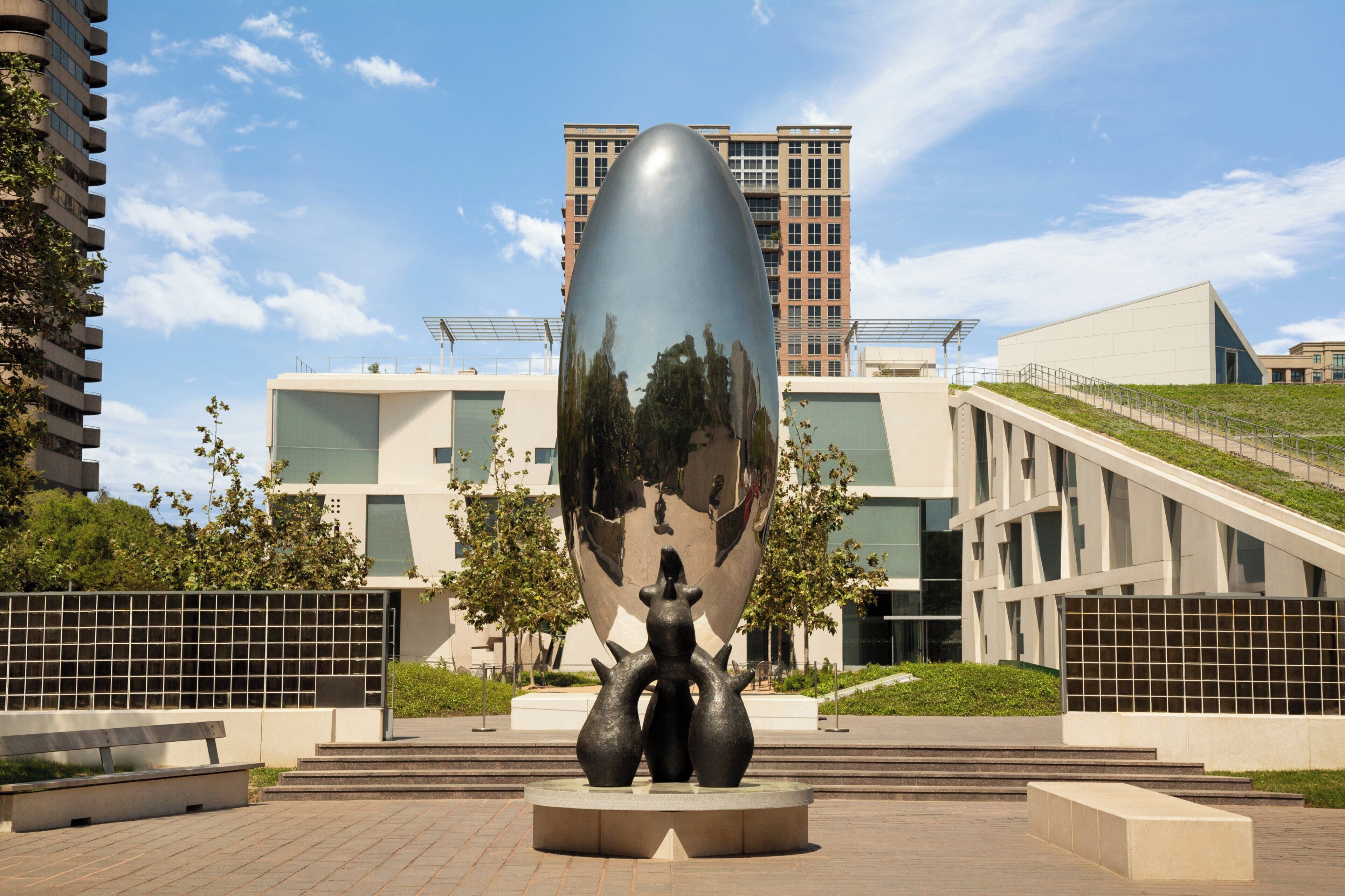 Uma escultura moderna com figuras abstratas em uma praça com escadas que levam a um edifício.