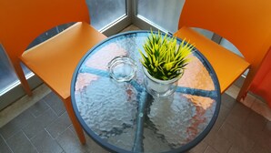 Uma mesa de vidro redonda com uma planta em vaso, duas cadeiras laranja e um vaso de vidro.