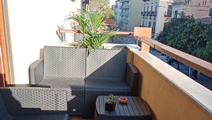 Uma varanda com móveis de vime, uma mesa pequena e um vaso com planta.