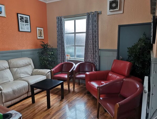 Uma sala de estar com um sofá bege, duas poltronas vermelhas, uma mesinha de centro preta e uma janela com cortinas.