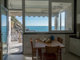 Uma área de refeições com vista para o mar e terreno rochoso através de grandes janelas.
