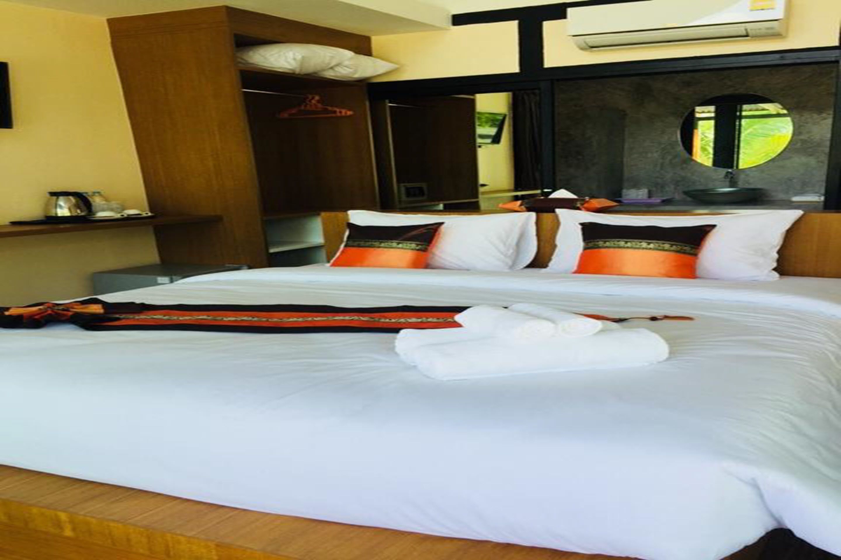 Quarto de hotel com uma cama grande, um guarda-roupa, uma mesa pequena com chaleira e vista para o verde através de uma janela redonda.