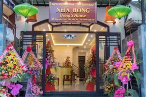 Entrada de hotel com uma placa indicando "Homestay Nha Bong Bong's House" e um balcão de recepção no interior.