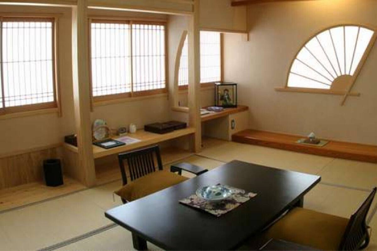 Um quarto japonês tradicional com tatames, uma mesa baixa com almofadas, uma porta deslizante e um leque na parede.