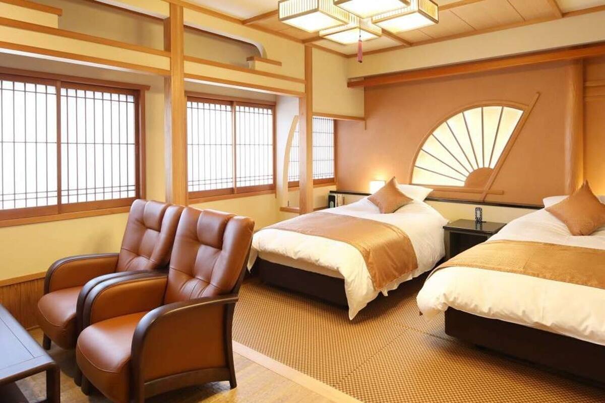 Quarto de hotel tradicional em estilo japonês, com tatames, duas camas com cabeceiras iguais, uma poltrona de couro marrom e um painel shoji.