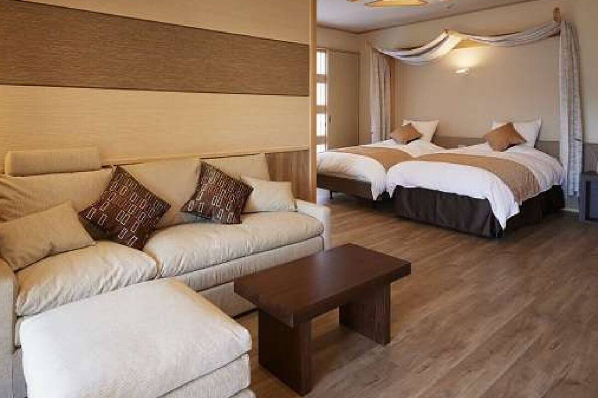 Quarto de hotel com sofá, cama, mesa de centro de madeira e cama com dossel.