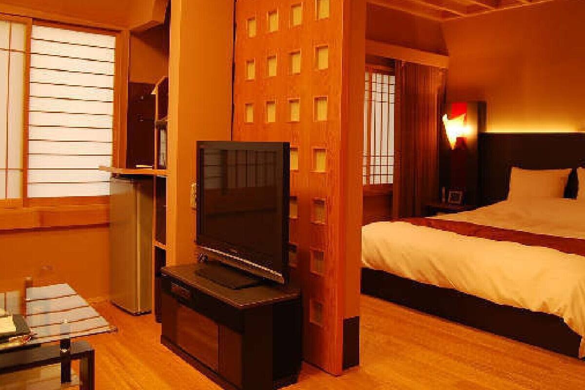 Quarto de hotel com cama, televisão, escrivaninha e janela com persianas.