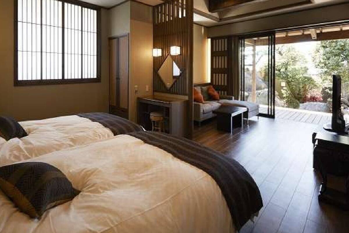 Quarto de hotel com duas camas, um sofá, uma TV e uma porta de vidro que se abre para o exterior.