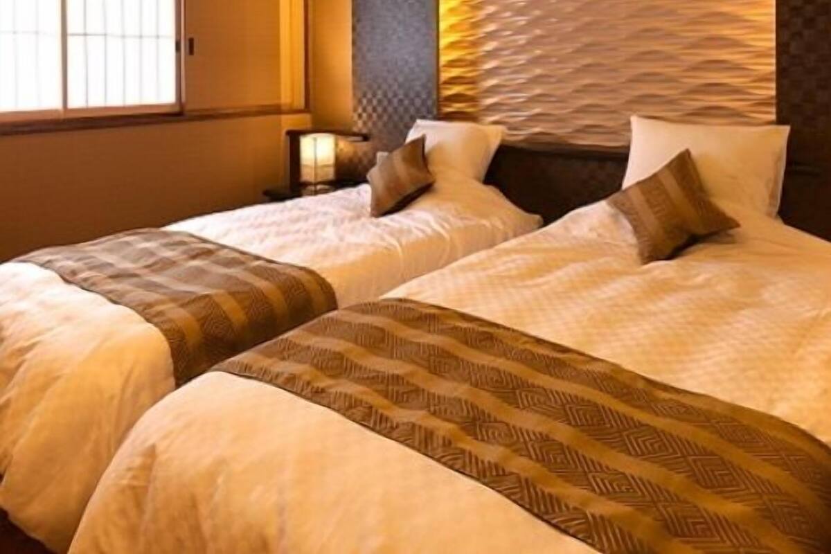 Quarto de hotel com duas camas, uma janela grande e uma parede texturizada.