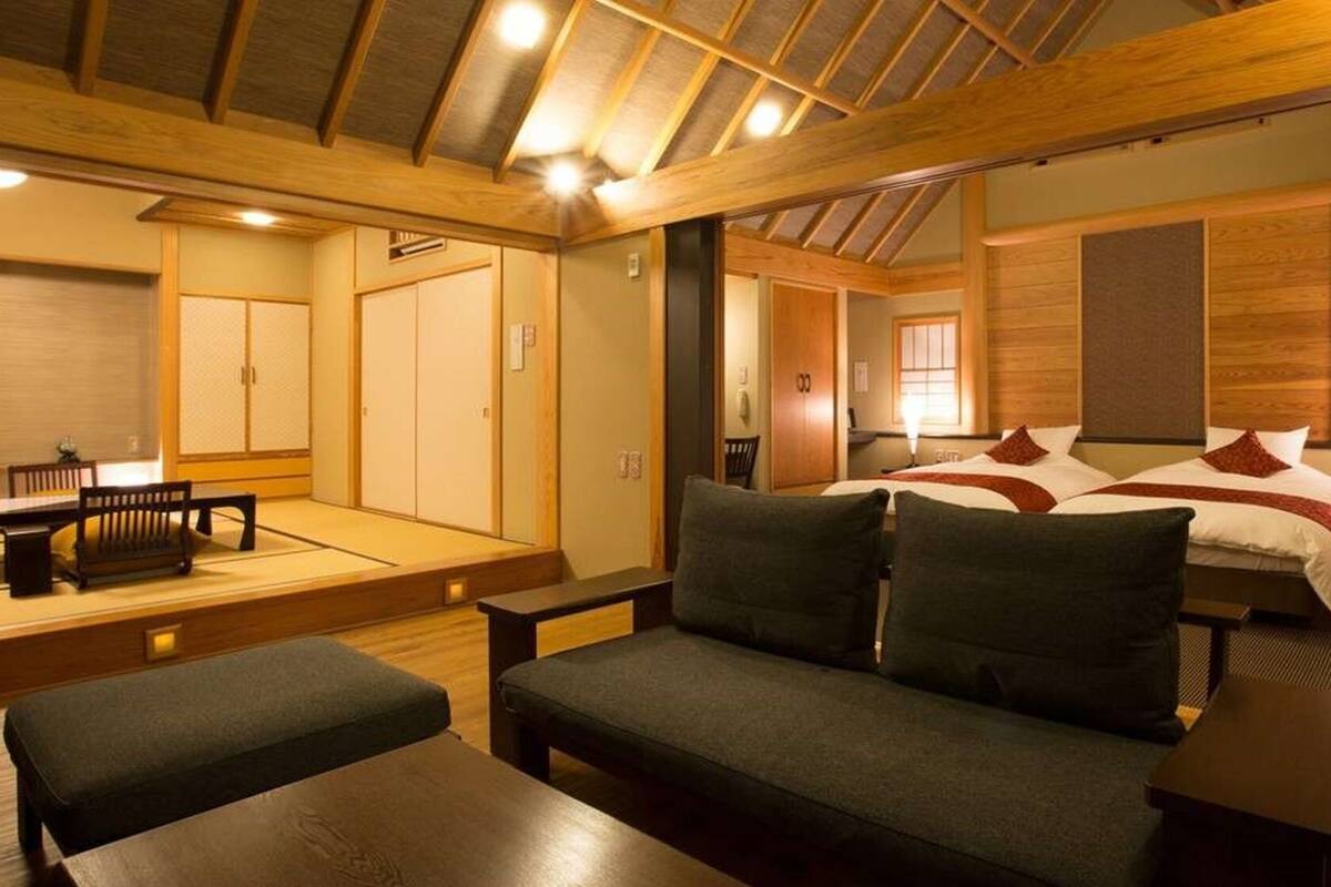 Quarto em estilo japonês tradicional com tatames, uma mesa baixa, um sofá e uma cama com detalhes vermelhos.