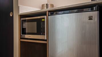 Um forno de micro-ondas Kenmore de aço inoxidável com visor digital e painel de controle, colocado sobre uma prateleira de madeira acima de uma geladeira de aço inoxidável.