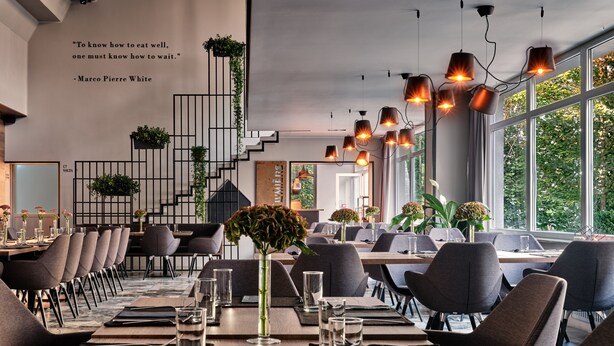 Um restaurante moderno com uma mesa de jantar comprida, várias cadeiras e luminárias pendentes.