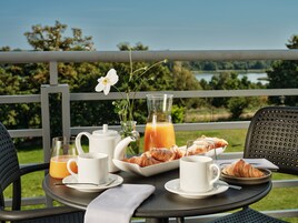 Uma mesa externa montada para o café da manhã, com vista para um lago e árvores.
