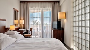 Quarto de hotel com uma cama grande, uma mesa de trabalho com cadeira, televisão e janela com cortinas.