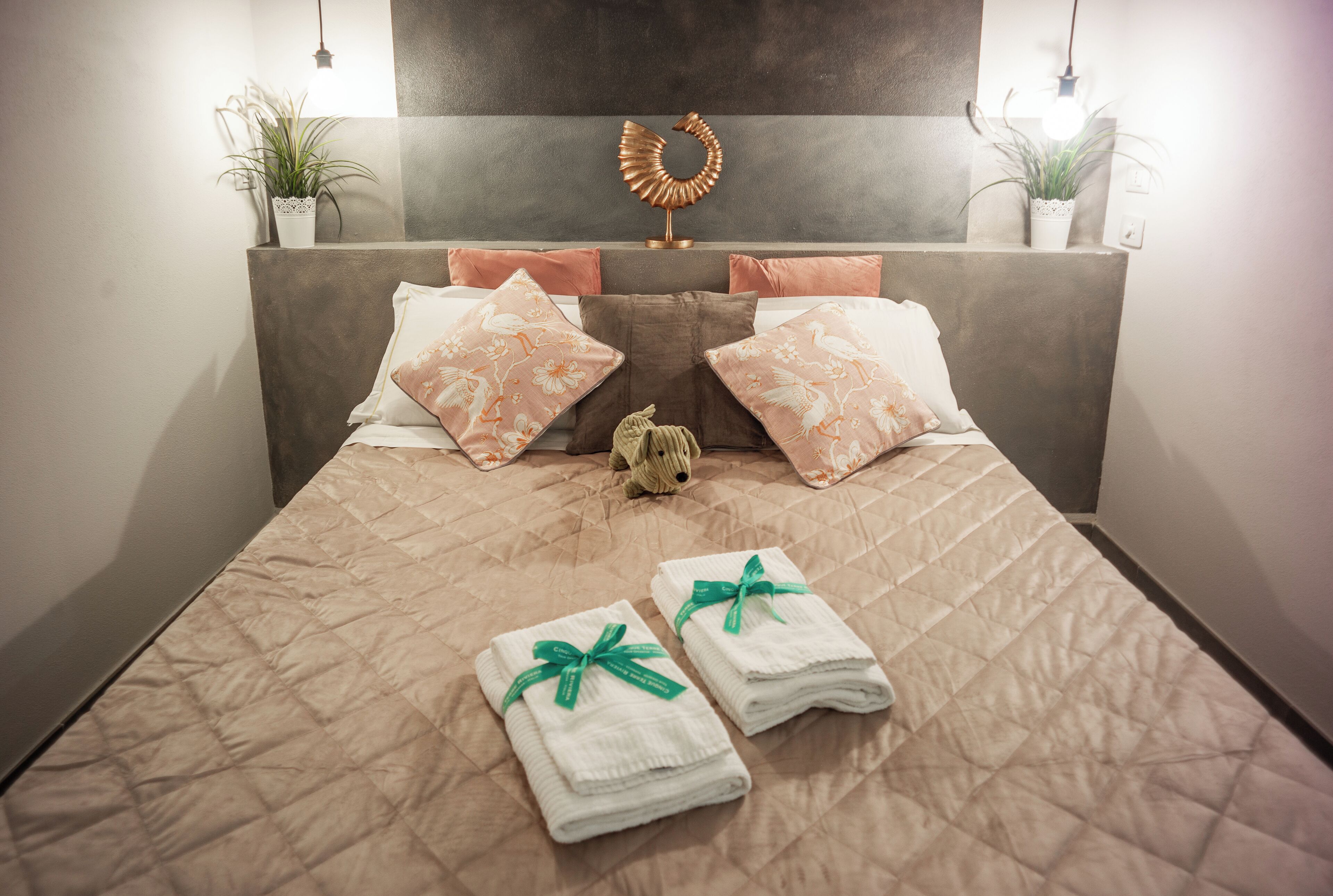 Uma cama bem arrumada com cobertura acolchoada, duas toalhas com fitas verdes e almofadas decorativas.