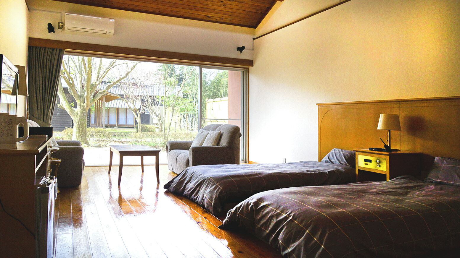 Quarto de hotel com duas camas, uma escrivaninha, uma cadeira, uma janela com vista para o exterior e uma mesinha.