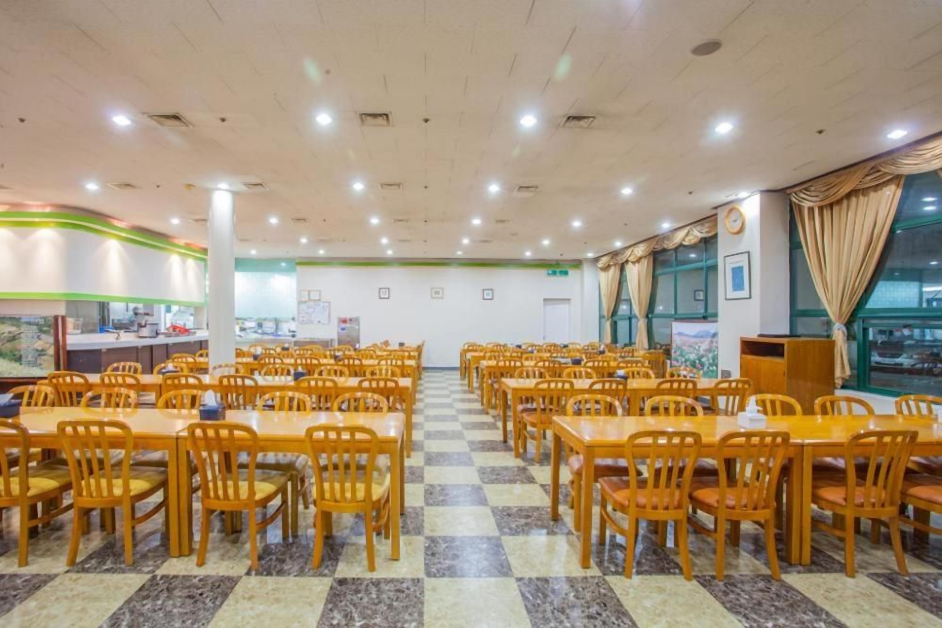 Uma ampla área de jantar com várias mesas e cadeiras, piso xadrez e vista através de grandes janelas.