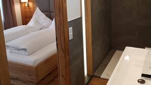Quarto de hotel moderno com cama de madeira, um espelho grande e uma banheira branca.
