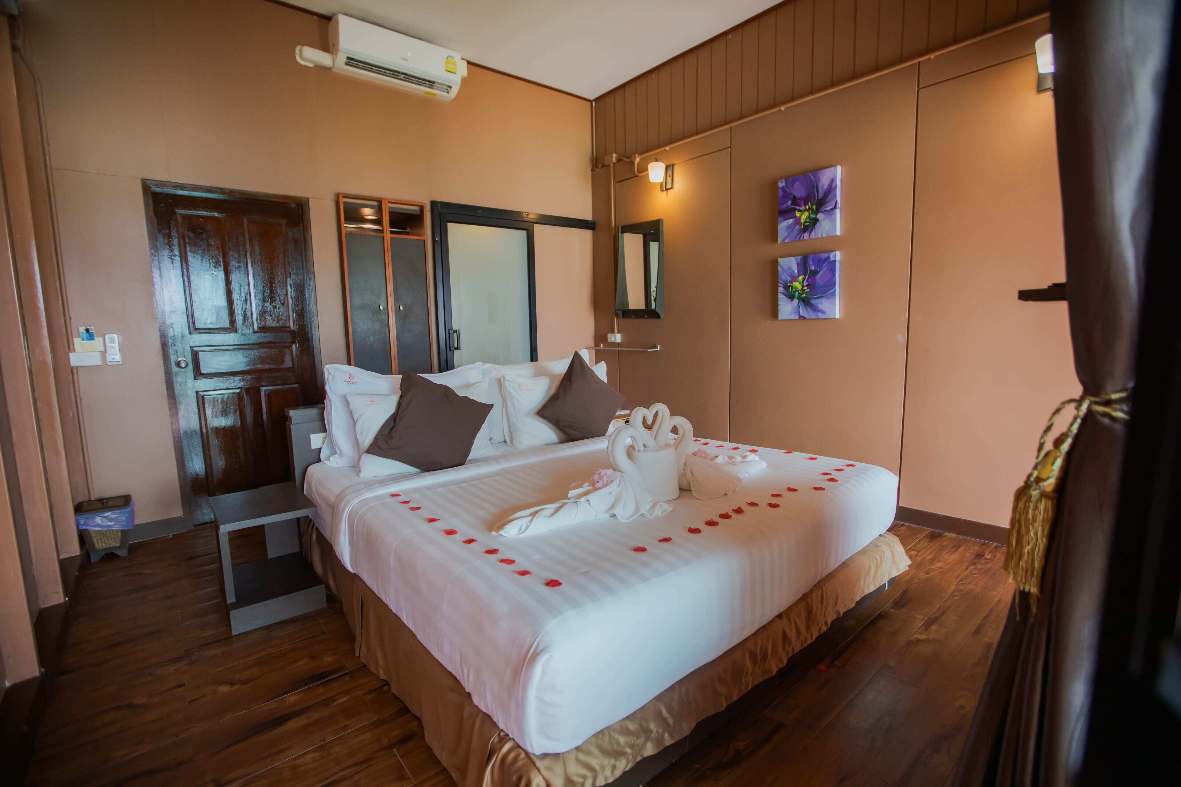 Quarto de hotel com piso de madeira, cama com roupa de cama branca, mesa de cabeceira, espelho e ar condicionado fixado na parede.