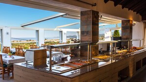 Buffet montado com vista para o mar, mobiliário de madeira e área de cozinha moderna.