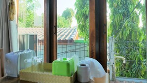 Um quarto com janela, uma caixa de lenços verdes, um rolo de papel higiênico e um dispensador de lenços em uma mesa.