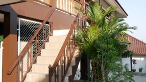 Um edifício de dois andares com escada de madeira, corrimão de metal e um vaso de planta.