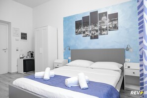 Quarto de hotel moderno com uma cama grande, uma escrivaninha e uma pequena cozinha equipada.