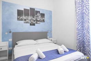 Quarto de hotel com cama, mesa de cabeceira, luminária na parede e cortina com padrão de zebra.