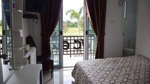 Quarto de hotel com cama, televisão, escrivaninha e varanda com vista para palmeiras.