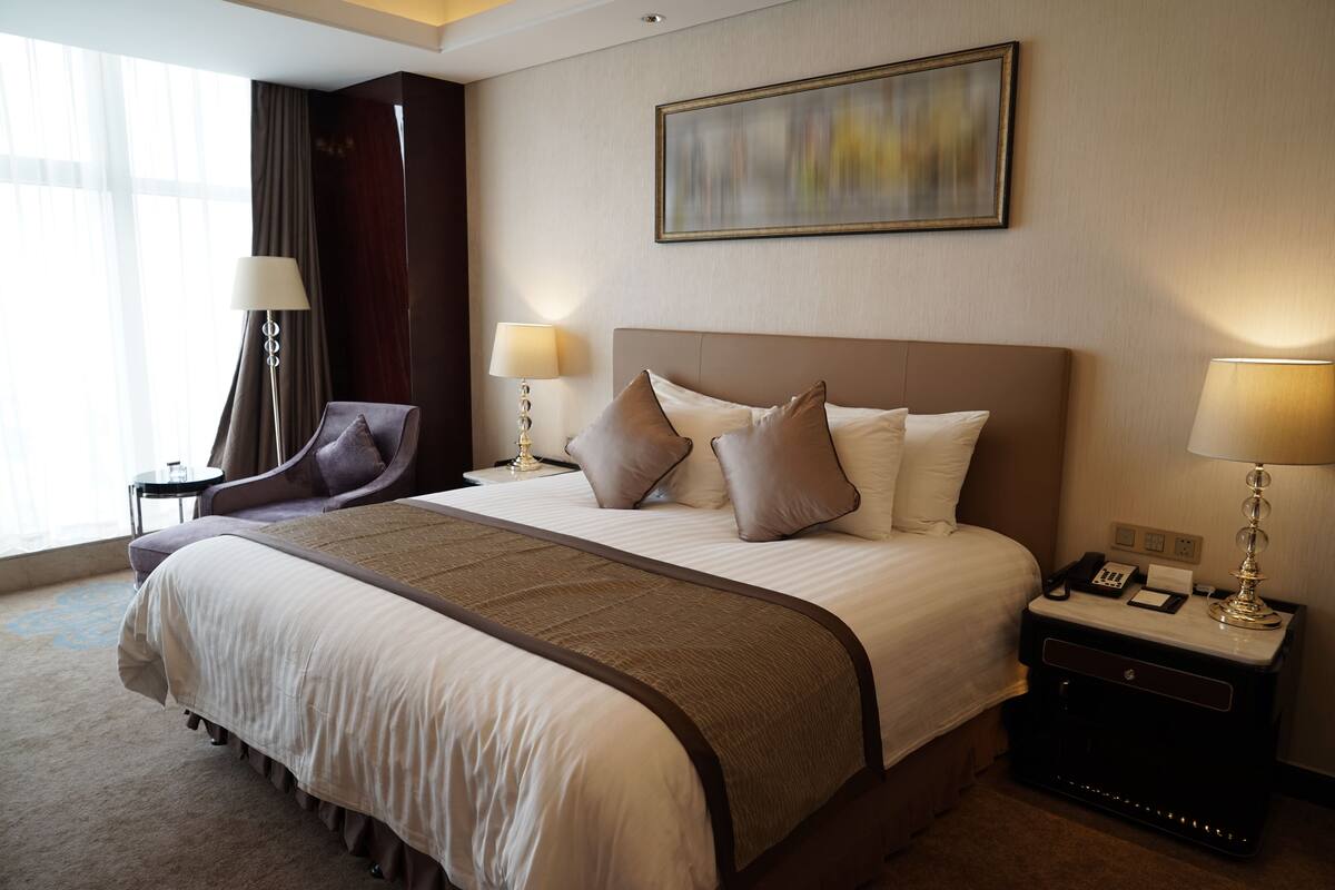 Quarto de hotel com uma cama grande, duas mesas de cabeceira, uma cadeira e um quadro na parede.