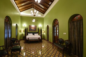 Quarto com cama grande, duas cadeiras, um candelabro e piso estampado.