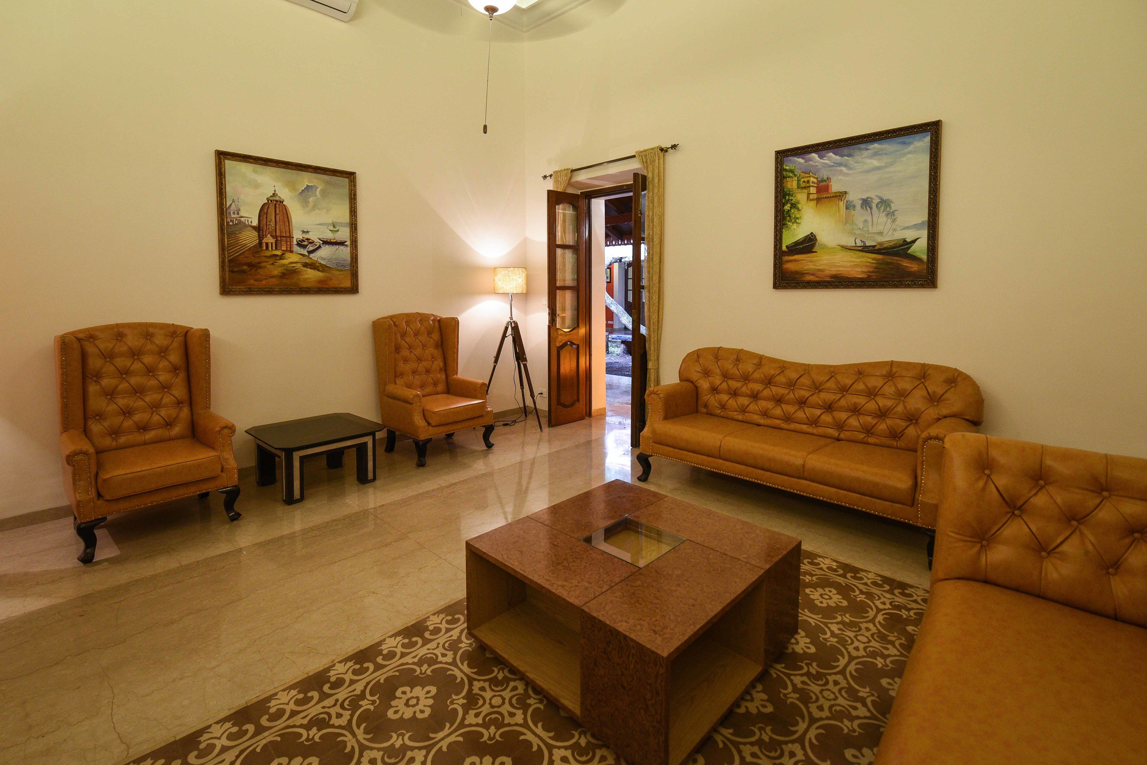 Uma sala de estar com um sofá, poltronas, uma mesa de centro e duas pinturas nas paredes.